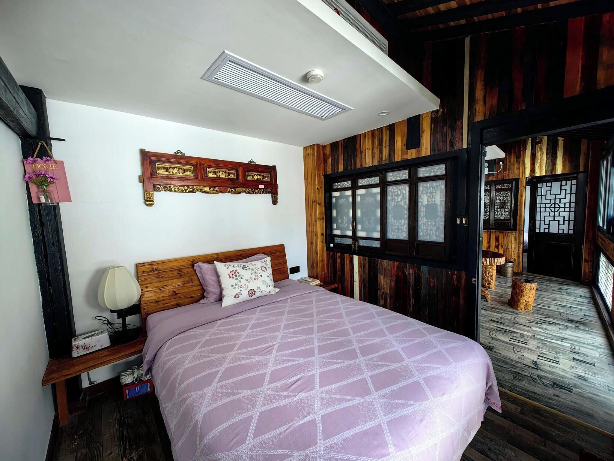Quarto com cama, mesa de cabeceira, abajur, um objeto decorativo na parede e vista para o interior de madeira.