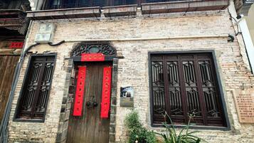 Um edifício tradicional com porta de madeira, duas janelas com grades decorativas e fachada de tijolos.