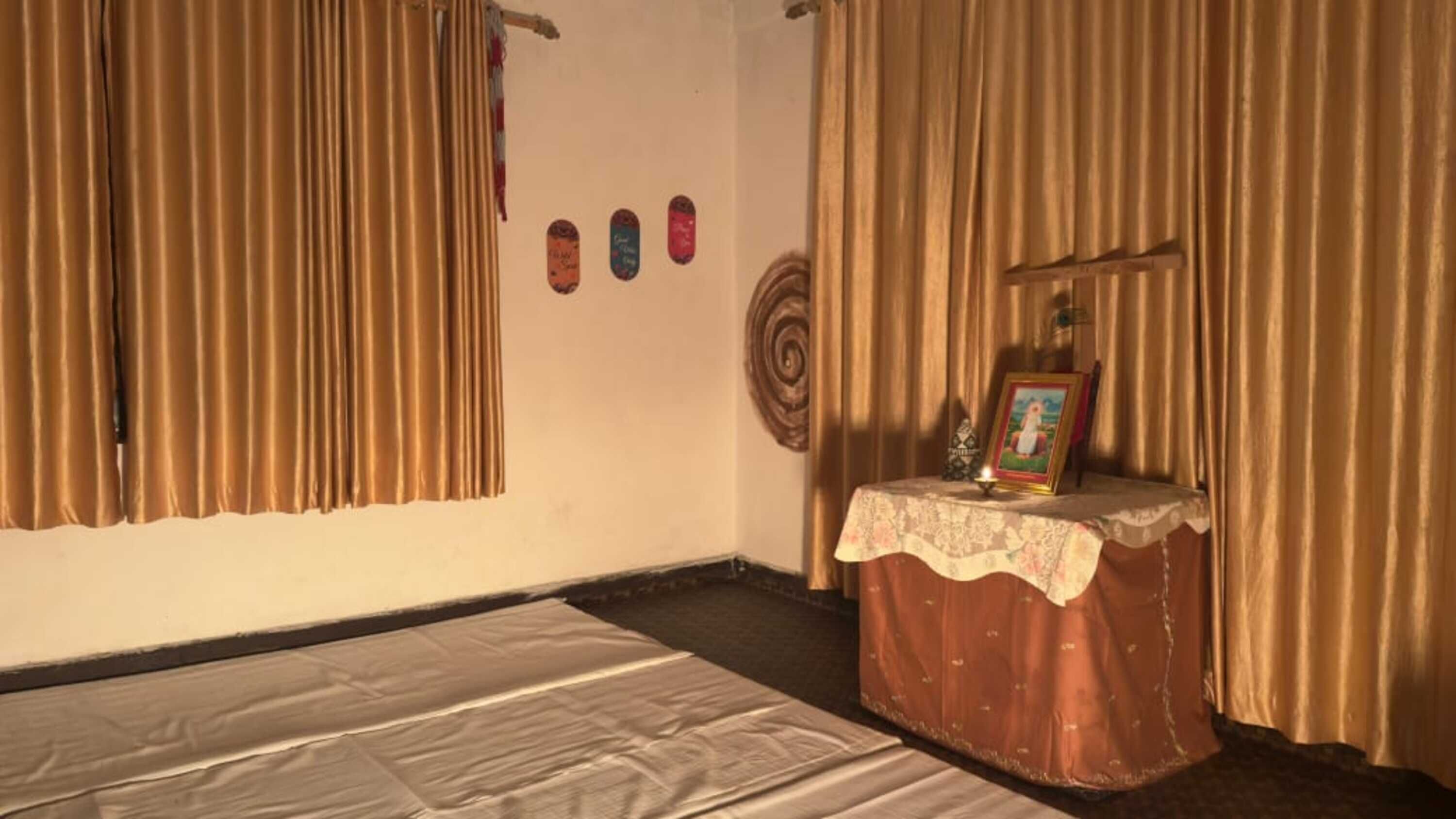 Quarto com uma cama, uma mesa pequena com porta-retrato e cortinas.