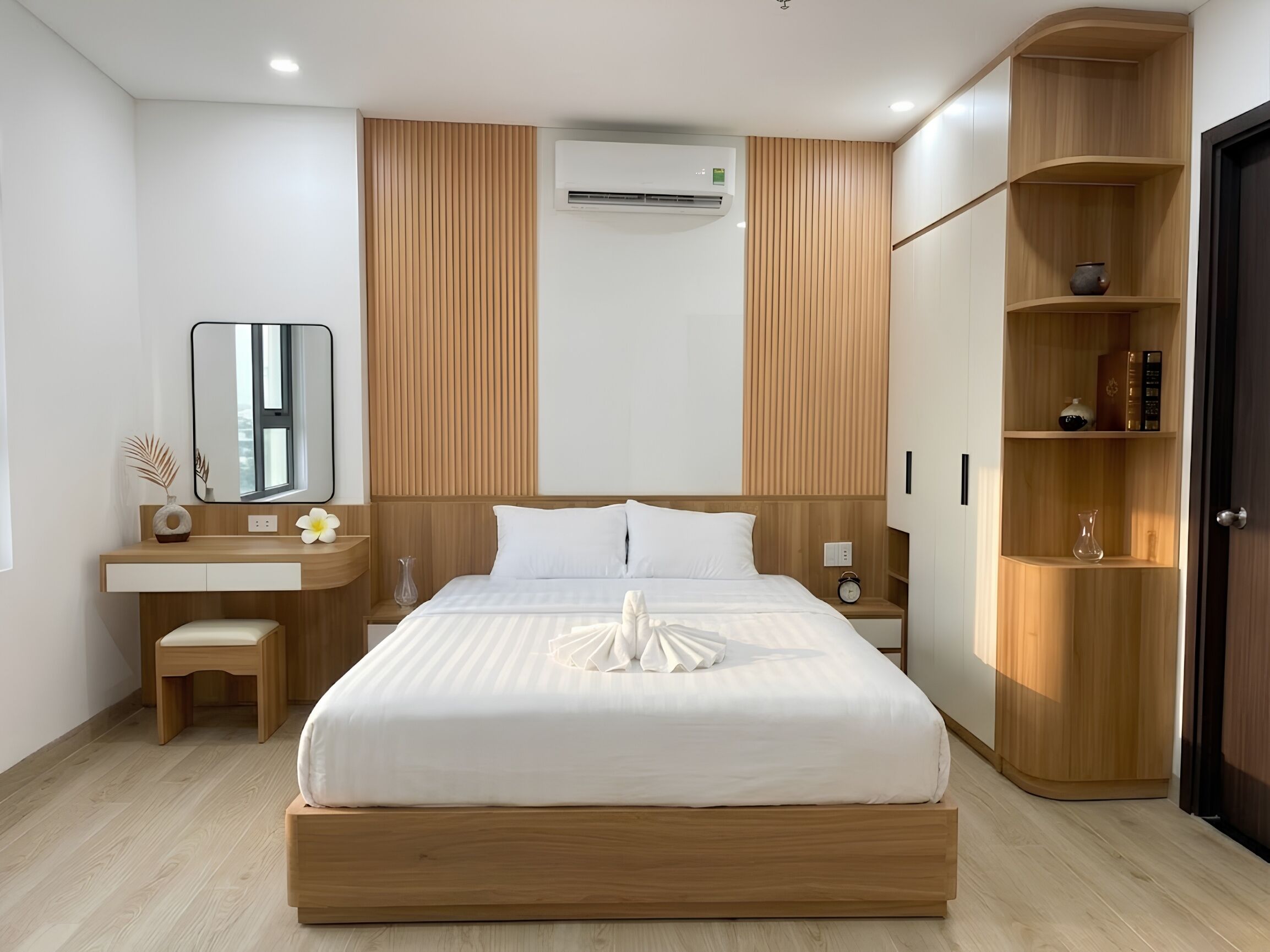 Quarto de hotel moderno com uma cama grande, um guarda-roupa de madeira, uma mesa de cabeceira com abajur e um ar condicionado instalado.