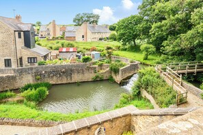 Uma ponte de pedra sobre um canal com uma pequena eclusa, rodeada por vegetação e edifícios de pedra tradicionais.