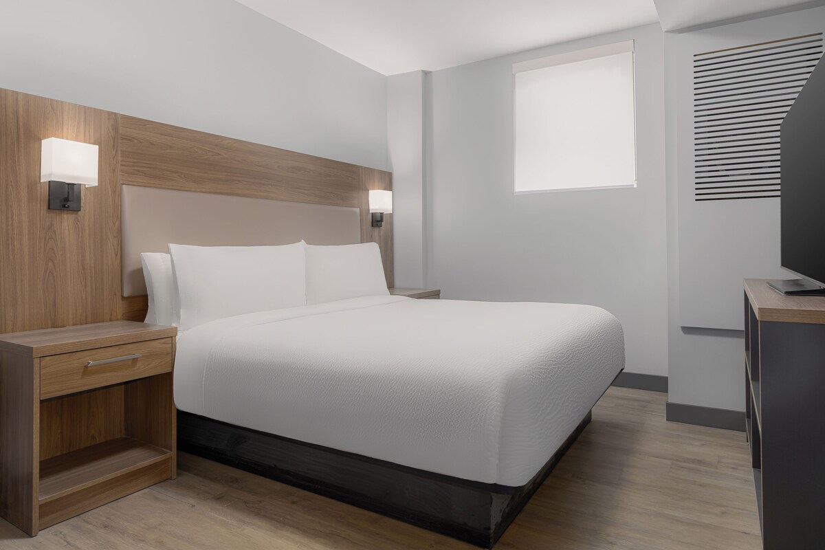 Quarto de hotel moderno com uma cama grande, mesas de cabeceira, escrivaninha e televisão.