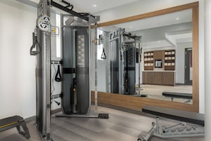 Uma academia com parede espelhada, equipamentos de musculação e um banco.