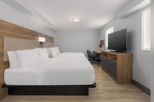 Quarto de hotel moderno com uma cama grande, uma escrivaninha, uma cadeira, uma televisão e uma janela.