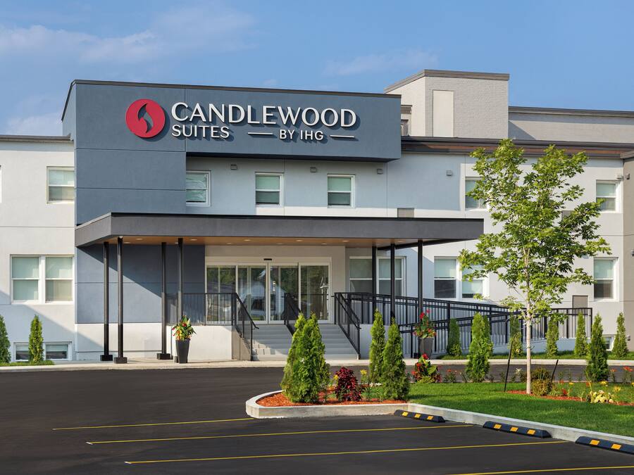 Entrada de um hotel com design moderno, exibindo um logotipo em destaque e o nome 'CANDLEWOOD SUITES BY IHG' acima da entrada.