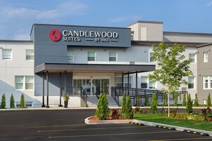 Entrada de um hotel com design moderno, exibindo um logotipo em destaque e o nome 'CANDLEWOOD SUITES BY IHG' acima da entrada.