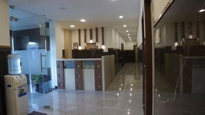 Uma área de recepção de hotel com um bebedouro, um balcão de recepção e um painel de vidro.