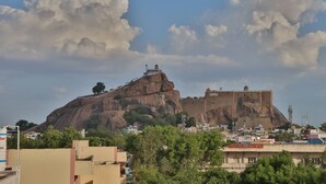 Uma grande formação rochosa com um edifício no topo, cercada por árvores e prédios.