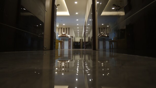 Corredor com piso espelhado, iluminação embutida e uma receção ao fundo.