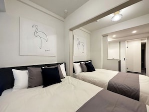 Quarto de hotel com duas camas, cada uma com cabeceira, roupa de cama branca e almofadas pretas e cinzentas. Há duas obras de arte emolduradas na parede, representando pássaros.