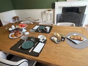 Uma mesa de jantar posta com pratos, tigelas, talheres e uma cafeteira, indicando um ambiente de café da manhã.