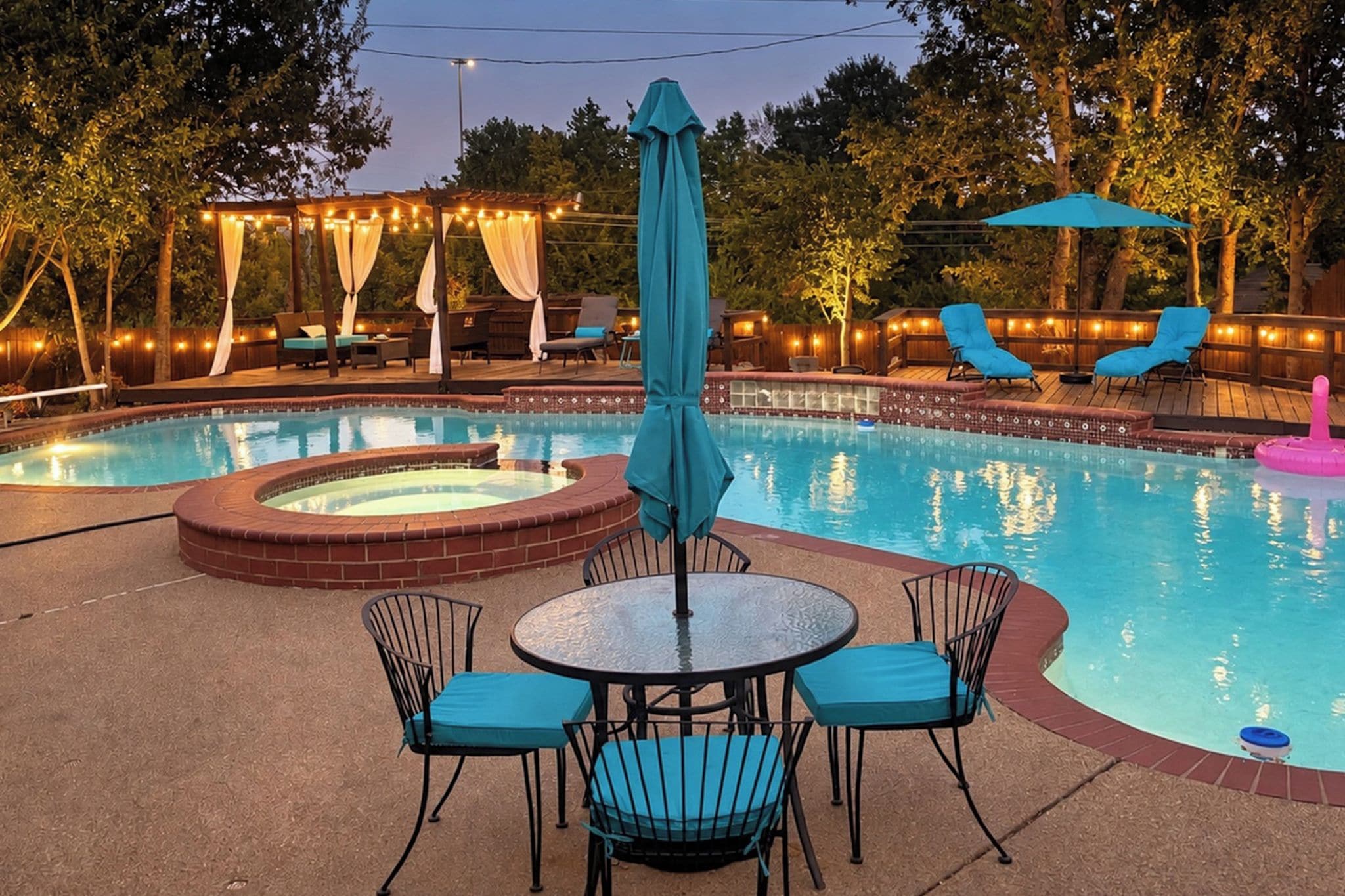 Piscina com hidromassagem, cercada por mobiliário de exterior e luzes de fadas.