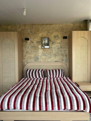 Quarto com parede de pedra, cama com roupa de cama listrada e um quadro na parede.