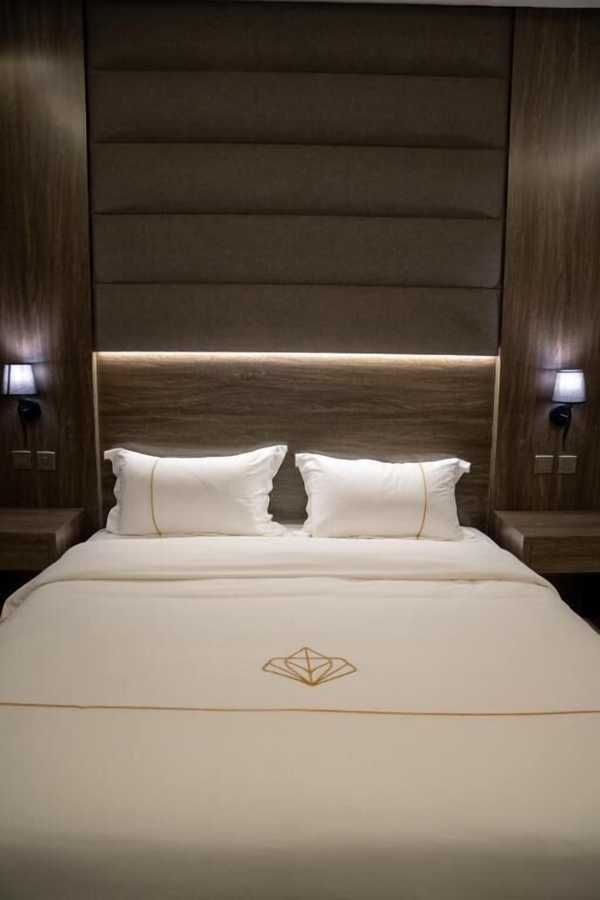 Quarto de hotel com uma cama grande, cabeceira de madeira e duas luminárias de cabeceira.
