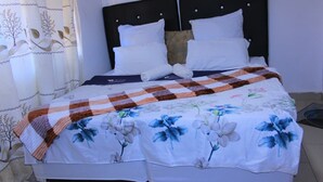 Uma cama de casal com colcha florida, duas almofadas brancas e um cobertor xadrez.