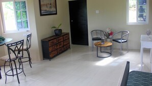 Um quarto com área de refeições, uma porta preta, um quadro e uma janela com vista.