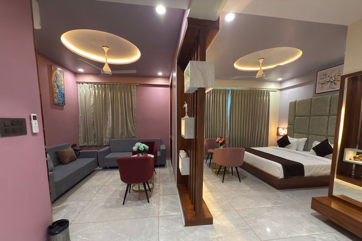 Quarto de hotel moderno com sofá, cadeiras, cama e área de jantar.