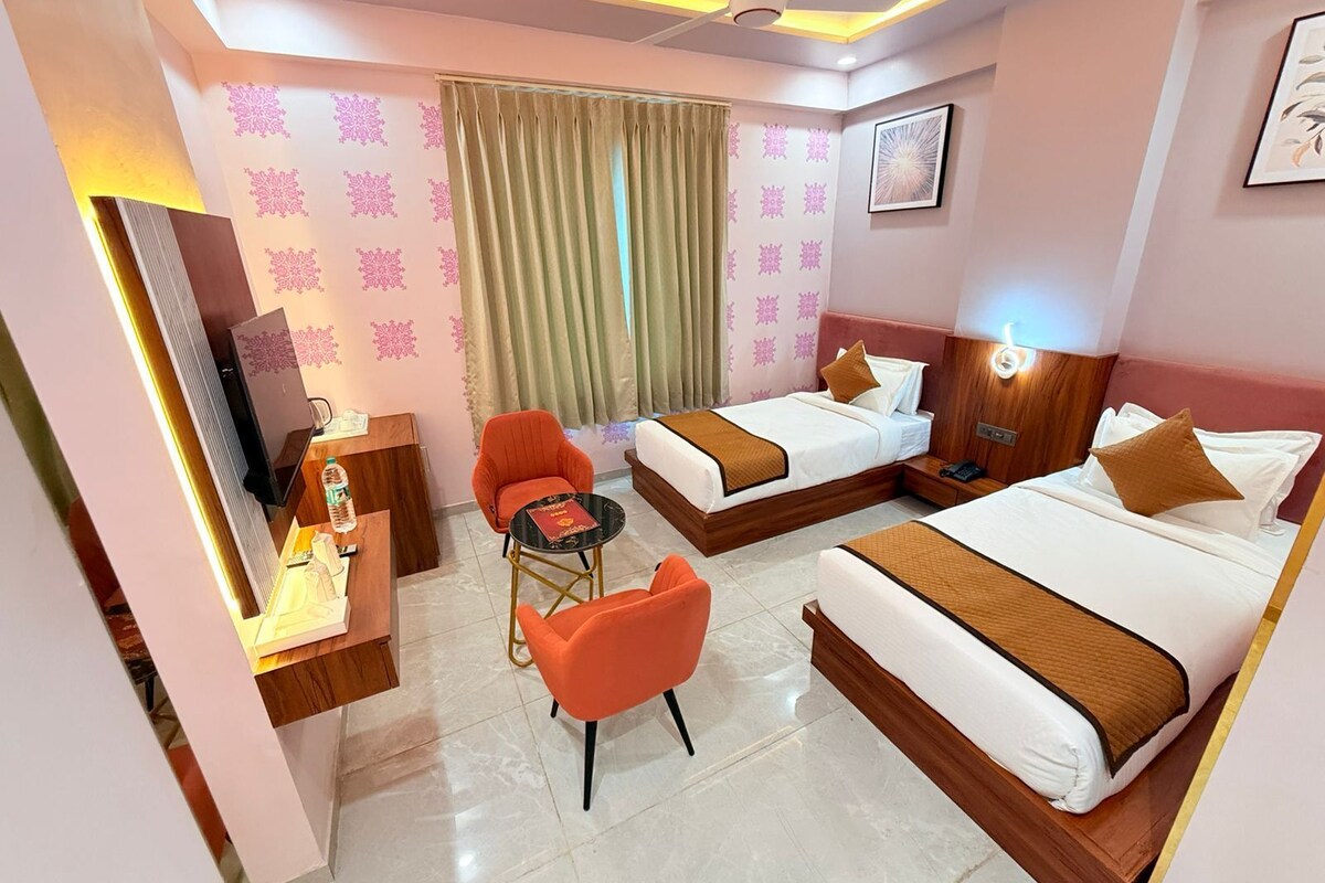 Quarto de hotel com duas camas, uma escrivaninha, uma cadeira, uma televisão e um ventilador de teto.