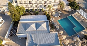 Um hotel com vários edifícios, piscina, área de estar ao ar livre e palmeiras.