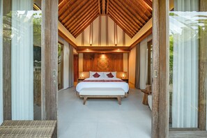 Um quarto com teto de madeira, uma cama grande com roupa de cama branca e duas luminárias de cabeceira.