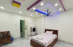 Quarto com cama, ventilador de teto, ar condicionado e um banquinho.