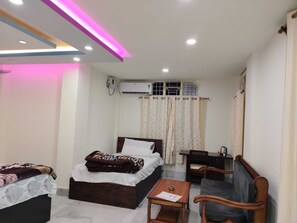 Quarto com cama, mesa de cabeceira, cadeira, mesinha e ar condicionado.