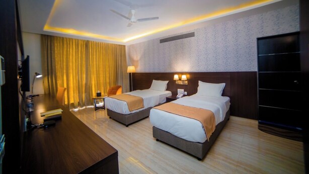 Quarto de hotel com duas camas, uma escrivaninha, uma cadeira, uma televisão e um ventilador de teto.