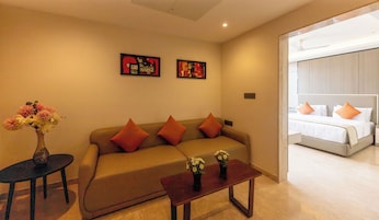 Quarto de hotel com sofá, uma pequena mesa com um vaso de flores e cama com almofadas.