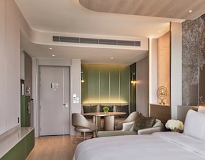 Quarto de hotel moderno com cama, área de estar e mesa de jantar.