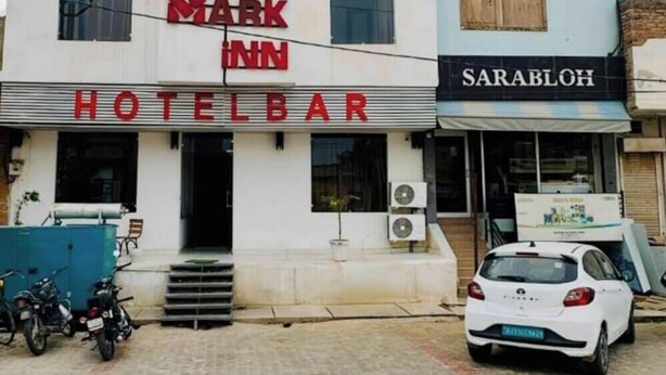 Um hotel com placas de 'Mark Inn Hotel Bar' e 'Sarabloh' em edifícios vizinhos.