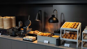 Um buffet de café da manhã com diversos alimentos, uma máquina de waffles e uma cafeteira.