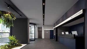 Uma área de recepção moderna com estação de auto-check-in, elevador de vidro e vista para a paisagem urbana.
