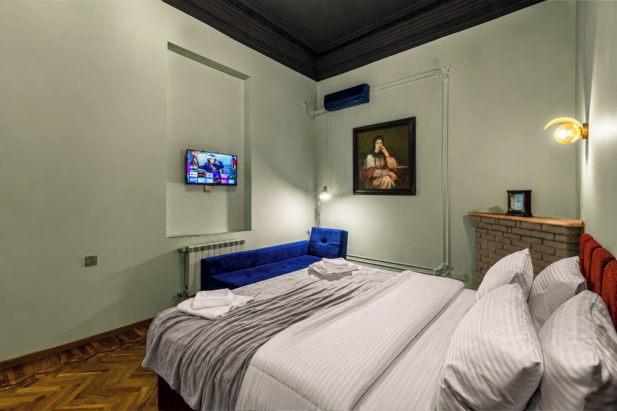 Quarto com cama, televisão, pintura e lareira.