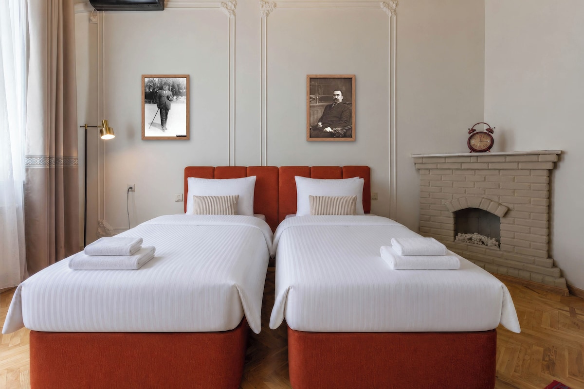 Quarto de hotel com duas camas, uma lareira e duas imagens emolduradas na parede.