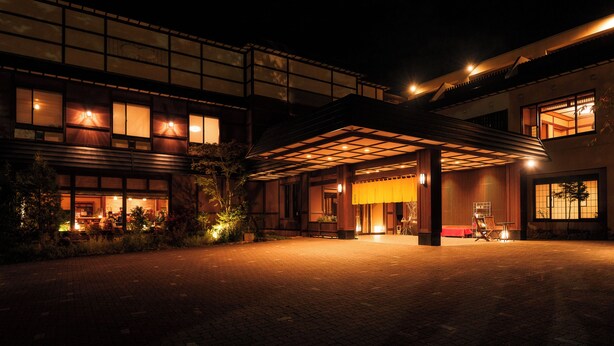 Entrada de hotel com galeria coberta, janelas amplas e fachada bem iluminada.