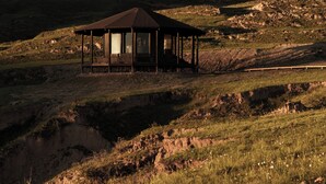 Uma construção isolada com telhado e paredes, localizada numa colina gramada sob um céu claro.