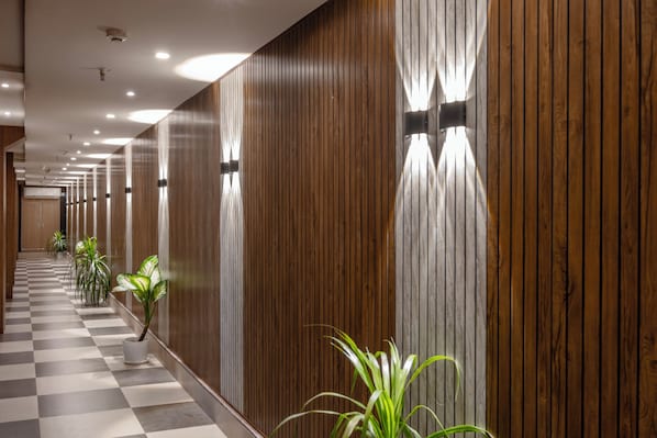 Corredor com paredes de painel de madeira, plantas em vasos e piso xadrez.