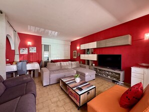 Uma sala de estar com sofá, mesa de centro, televisão e área de jantar com mesa e cadeiras.