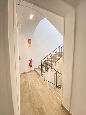 Corredor que leva a uma escadaria, com um extintor fixado na parede.