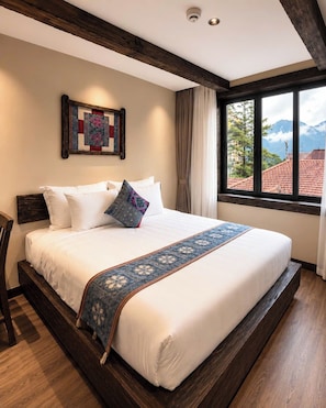 Quarto de hotel com uma cama grande, vista para as montanhas e teto de madeira.