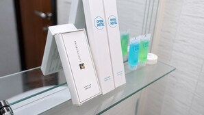 Casa de banho com prateleira de vidro exibindo um kit de higiene e produtos de higiene pessoal da marca do hotel.