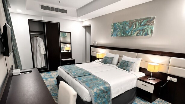 Quarto de hotel com cama, mesas de cabeceira, escrivaninha, cadeira, guarda-roupa e um quadro na parede.