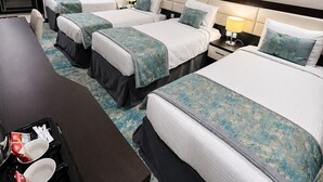 Quarto de hotel com três camas, uma escrivaninha com um conjunto de objetos e um quadro na parede.