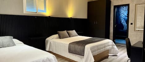 Quarto de hotel com duas camas, um guarda-roupa, uma escrivaninha e uma televisão.