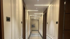 Um corredor comprido e estreito com piso de mármore polido, iluminação embutida e portas em ambos os lados.