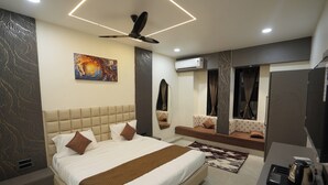 Quarto de hotel moderno com uma cama grande, um ventilador de teto, ar condicionado, área de estar e televisão.