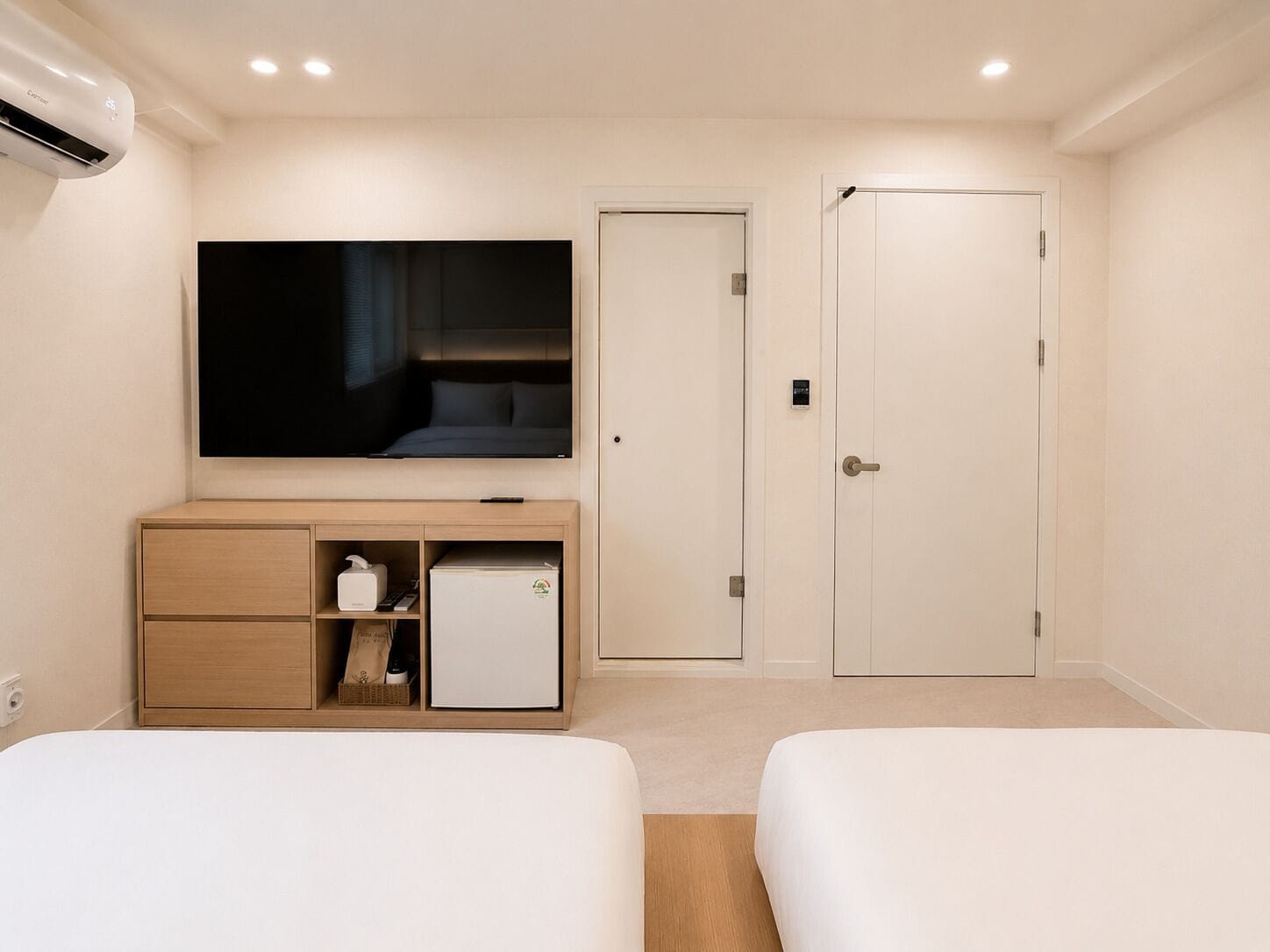 Quarto de hotel com duas camas, televisão, minibar e uma porta.