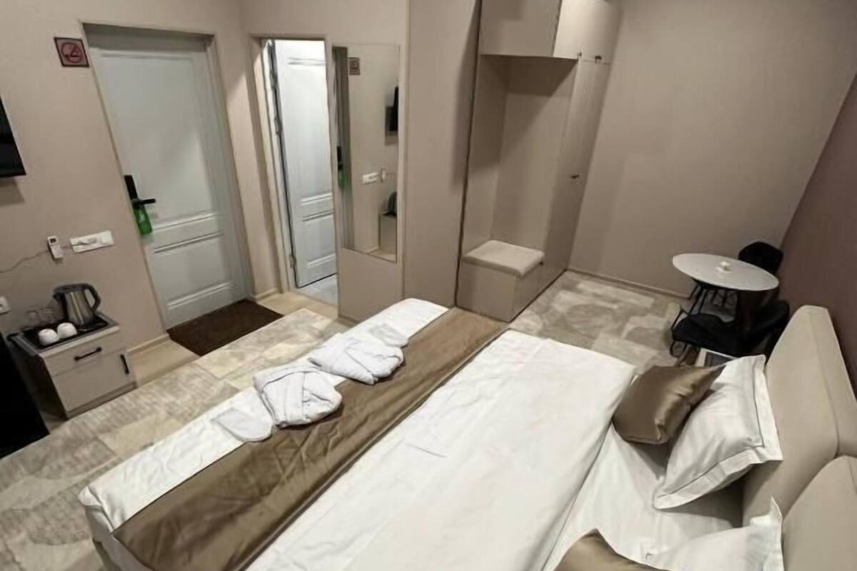 Quarto de hotel com cama, mesa de cabeceira, cadeira, espelho e porta.