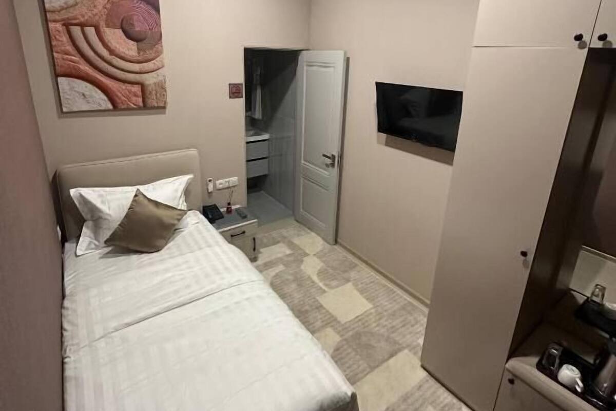 Quarto de hotel com cama, escrivaninha, guarda-roupa, televisão e espelho.