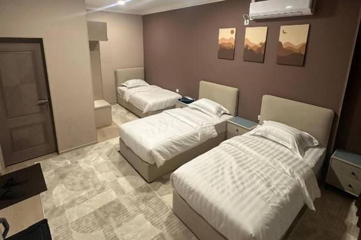 Quarto de hotel com duas camas, uma escrivaninha, uma cadeira, ar condicionado e uma porta.